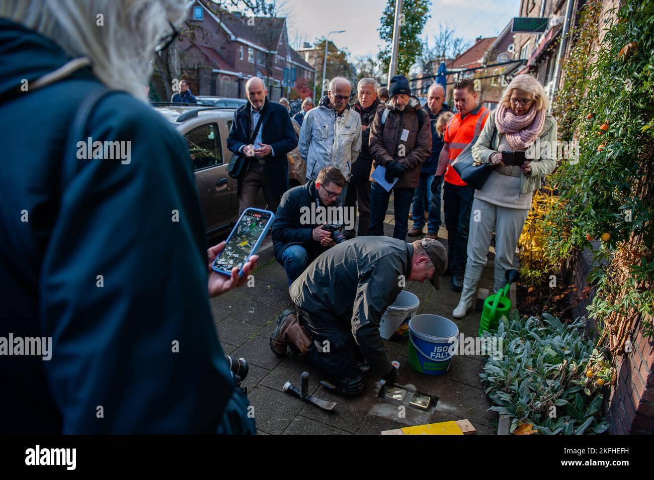 People gather around a man placing the stones on the pavement. As the ...