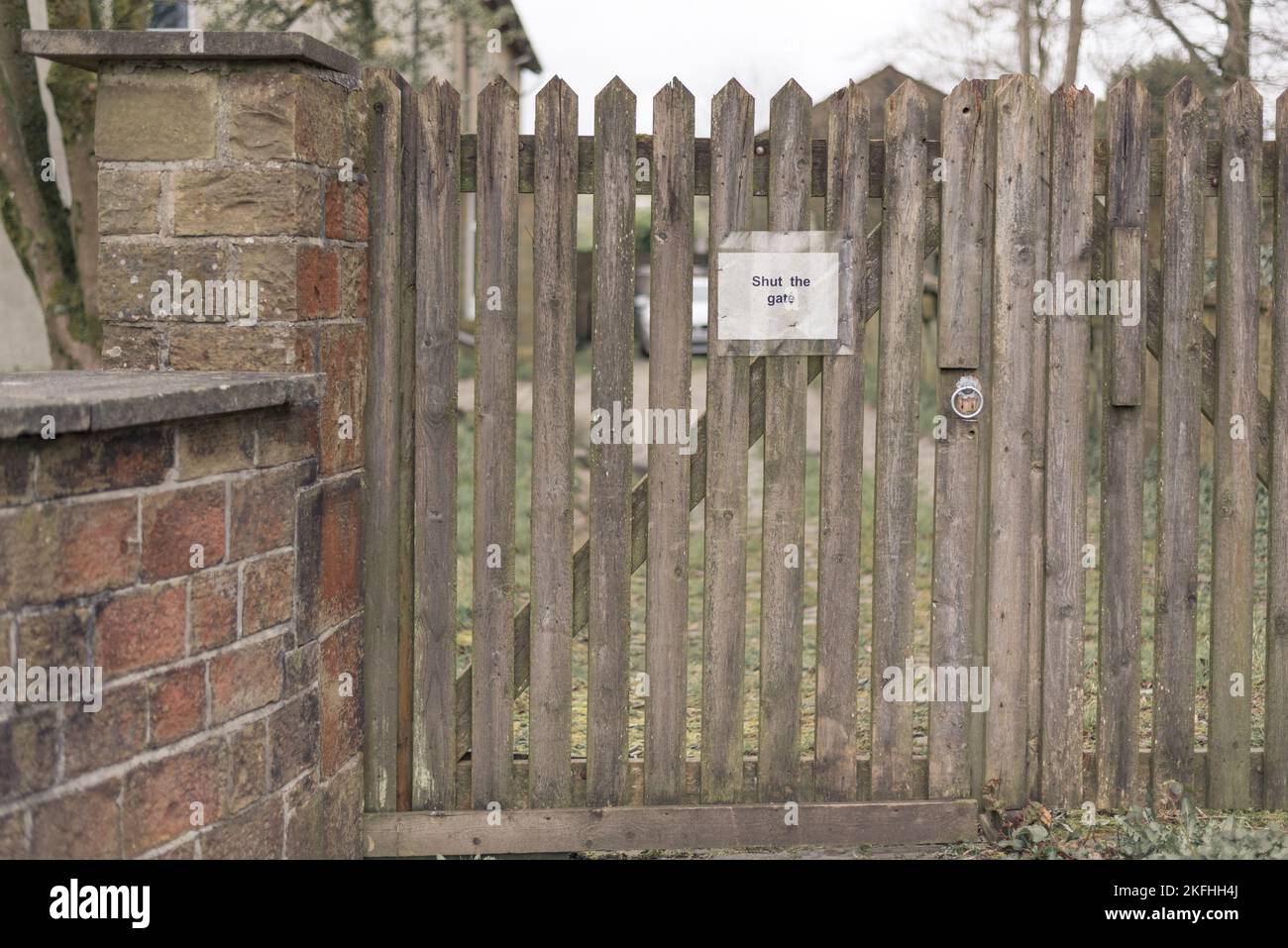 Old wooden gate with sign which reads shut the gate. Rotting wood along ...