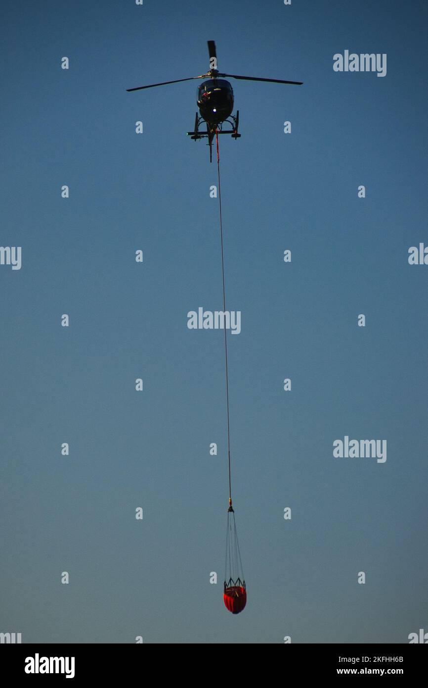 A vertical shot of a fire force helicopter carrying water on blue sky ...