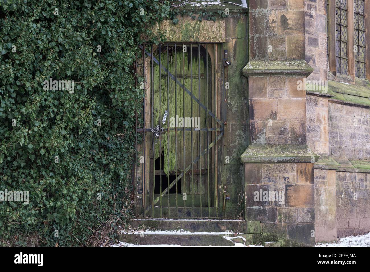 Old derelict church door with green mold and over grown ivy climbing ...