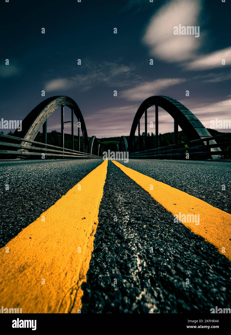 A bridge with two yellow lines on the asphalt road under a cloudy sky ...