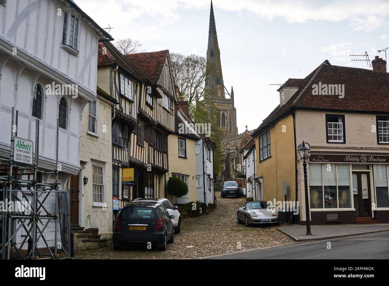 Narrow cobbled street with old beamed buildings and a church spire at ...