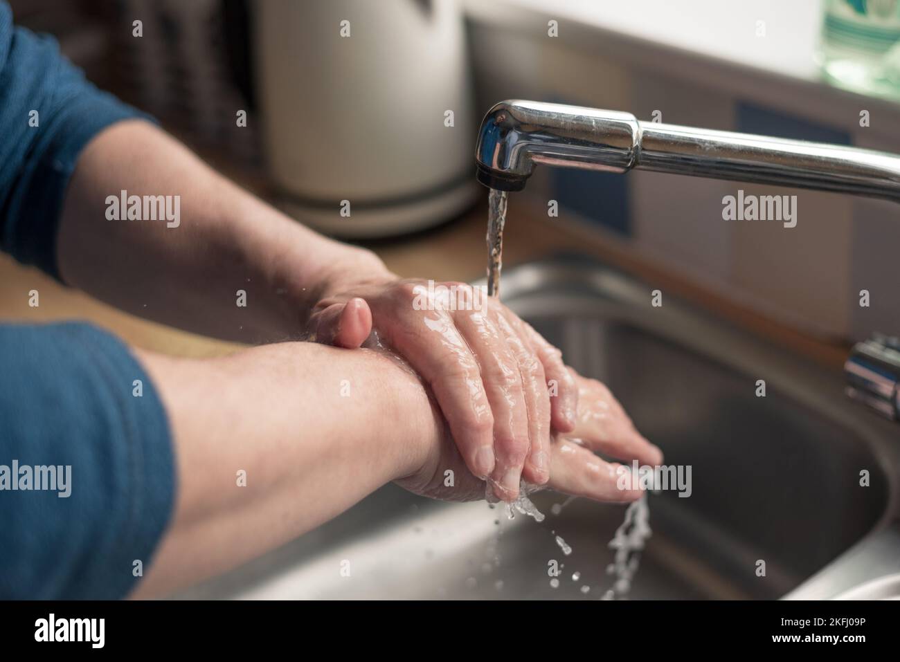 Man washing his hands with soap and water with the tap water running ...
