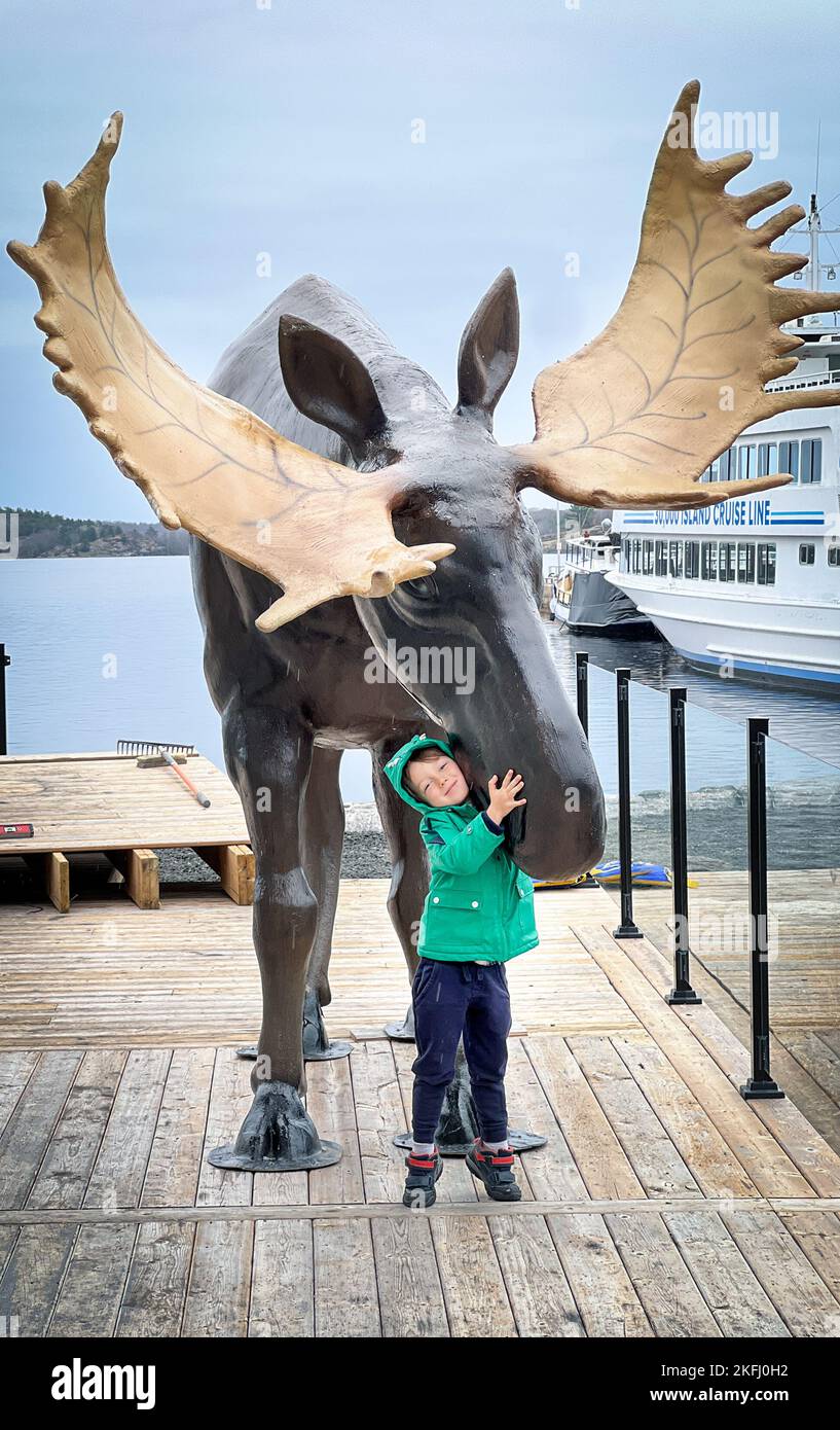 Full length of Caucasian boy wearing winter coat embracing moose statue ...
