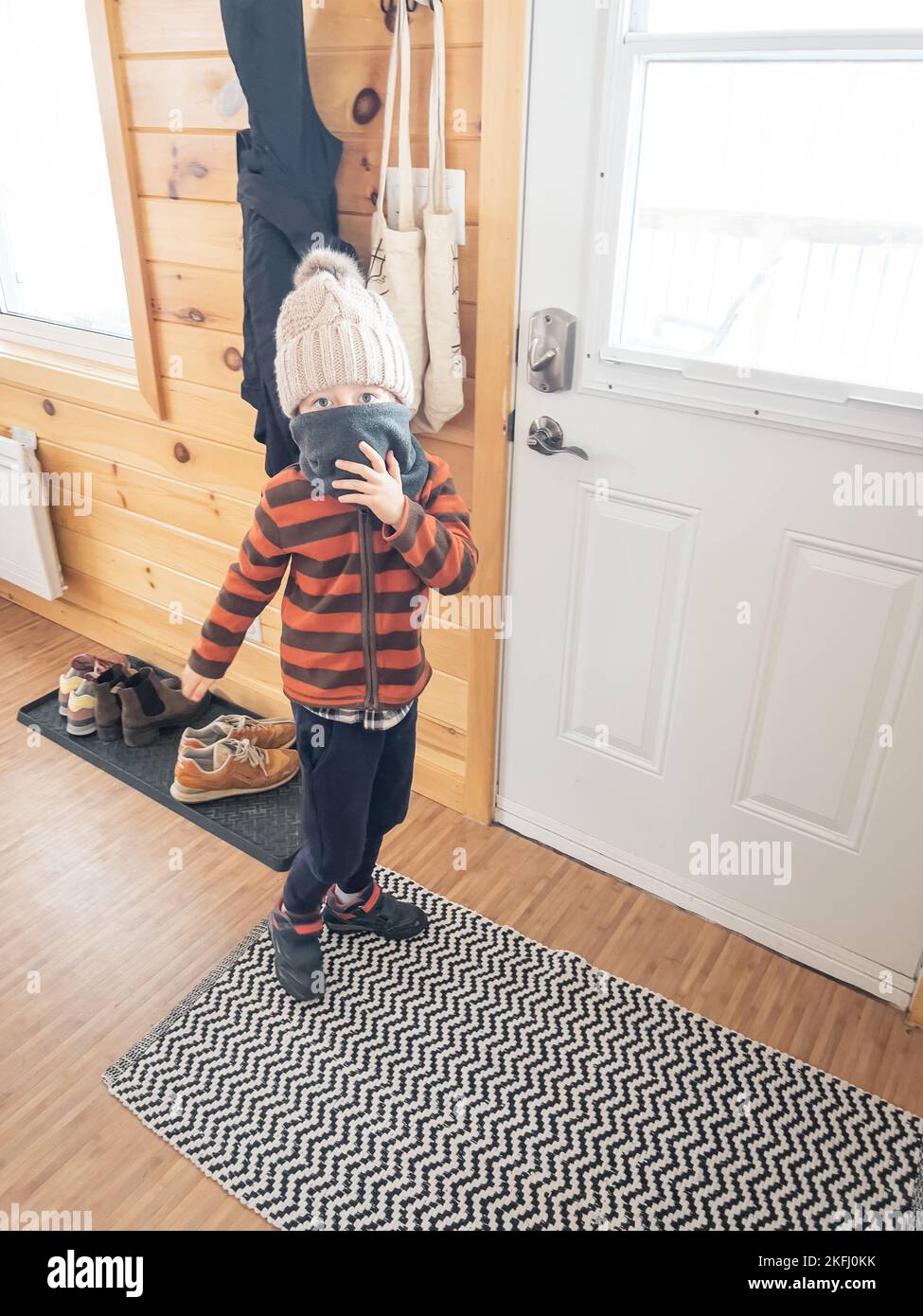 Portrait of playful Caucasian boy hiding face with scarf while standing ...
