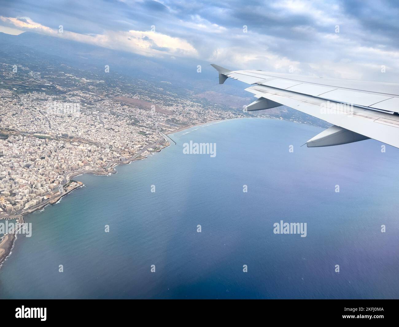 Cropped image of airplane wing flying over seascape and cityscape ...
