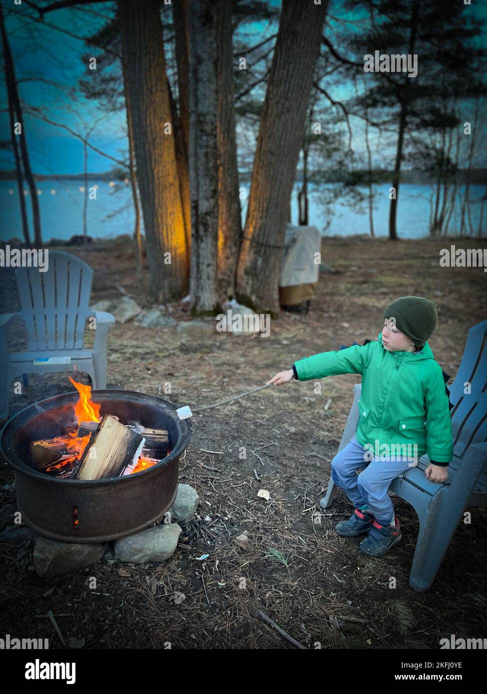 Caucasian boy roasting marshmallow over campfire while sitting on ...