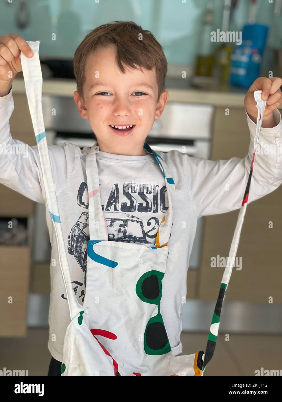 Portrait of cheerful cute caucasian boy wearing apron holding textile ...