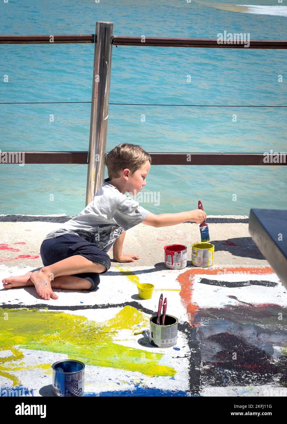 Boy painting on concrete walkway. Male child is dipping brush in paint ...