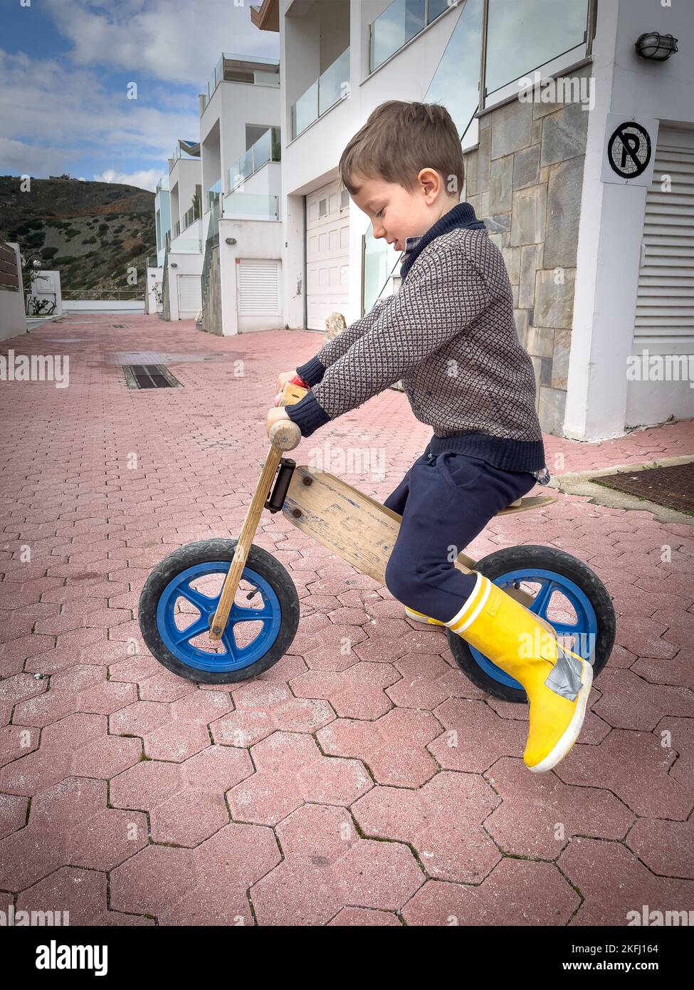 Side view of playful Caucasian boy wearing rubber boots riding bicycle ...