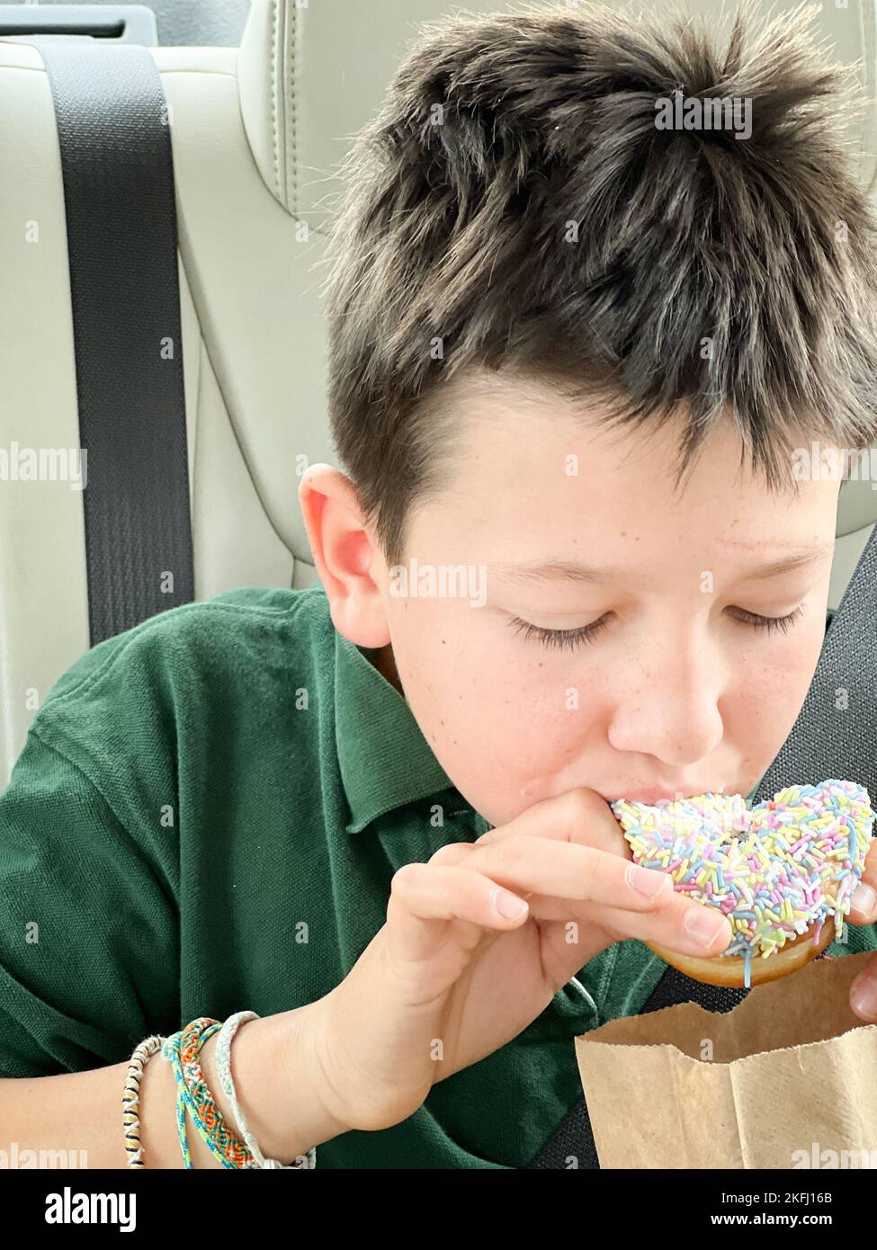 Close-up of cute caucasian boy eating doughnut with colorful sprinkles ...