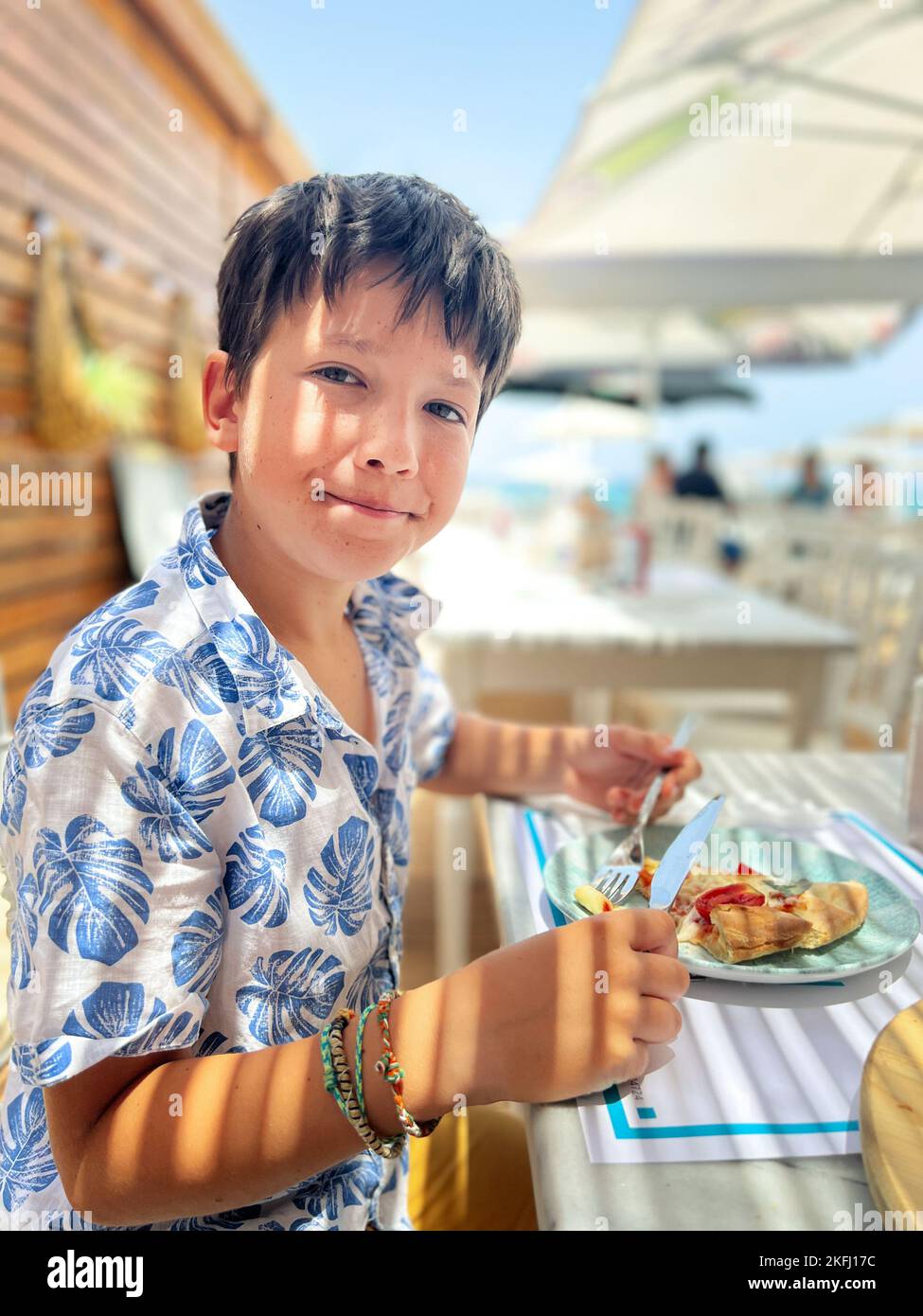 Portrait of cute smiling Caucasian boy eating pizza slice on table ...