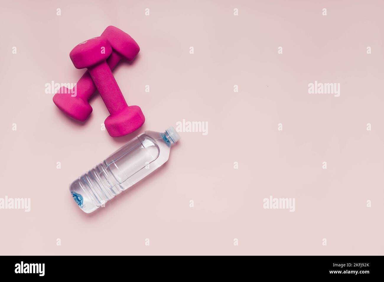 Pink dumb bell weights with bottled water on pink background new years ...