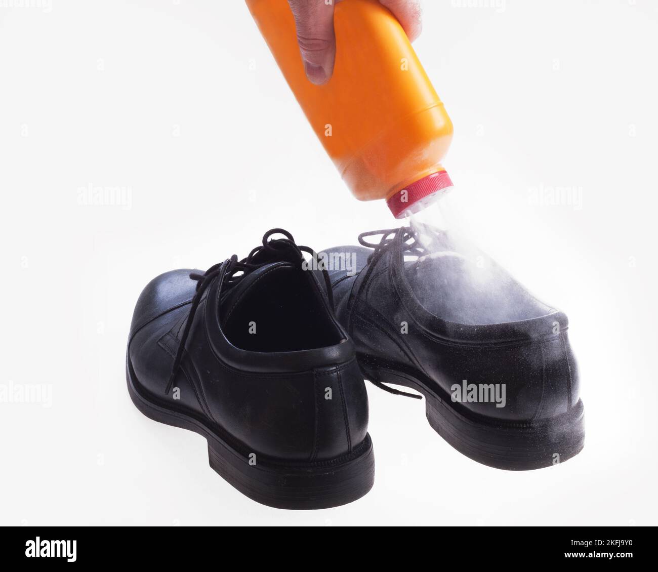 A hand pouring foot powder onto a pair of black leather shoes on a ...