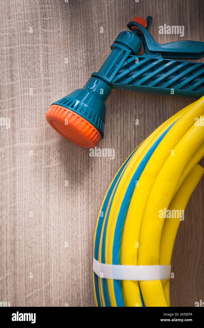 Hand spraying rubber garden hose with spray nozzle on wooden board ...