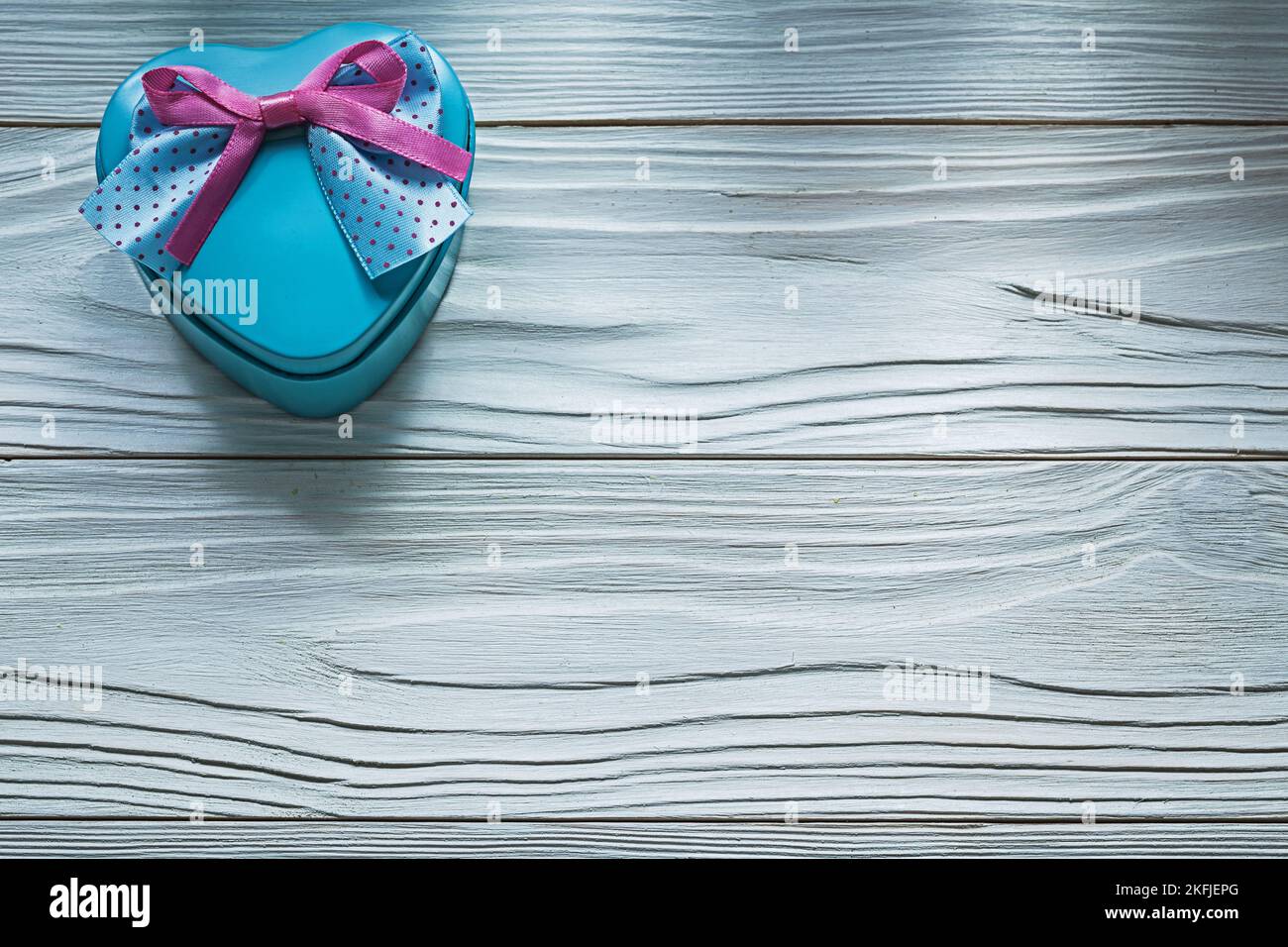 Heart-shaped blue present box with pink bow on wooden board holidays ...