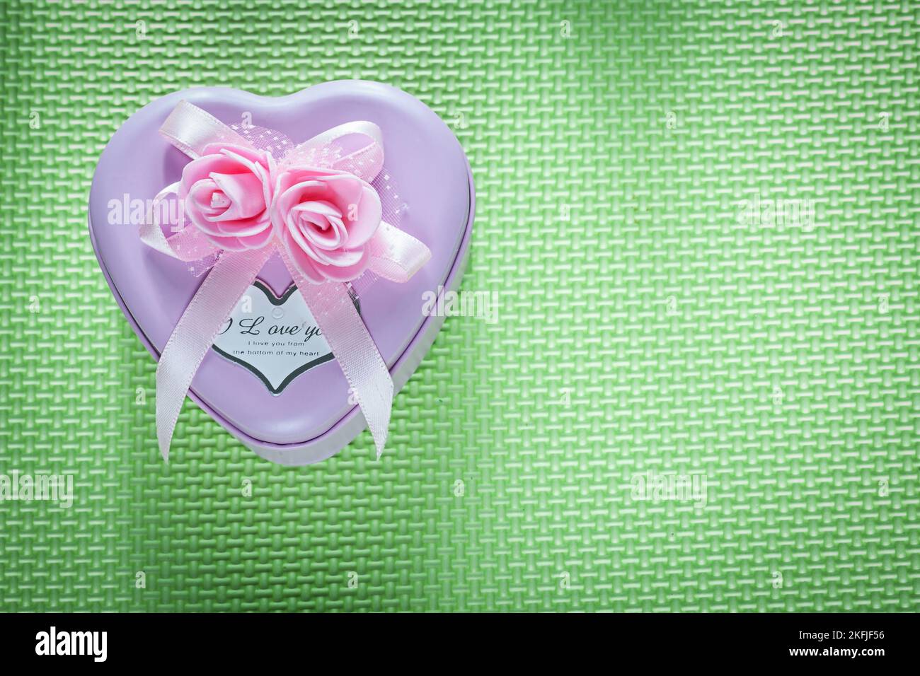 Metal purple heart-shaped present box with bow on green background ...