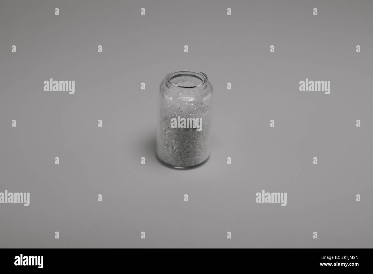 White color glitter powder in a small glass bottle isolated on grey ...