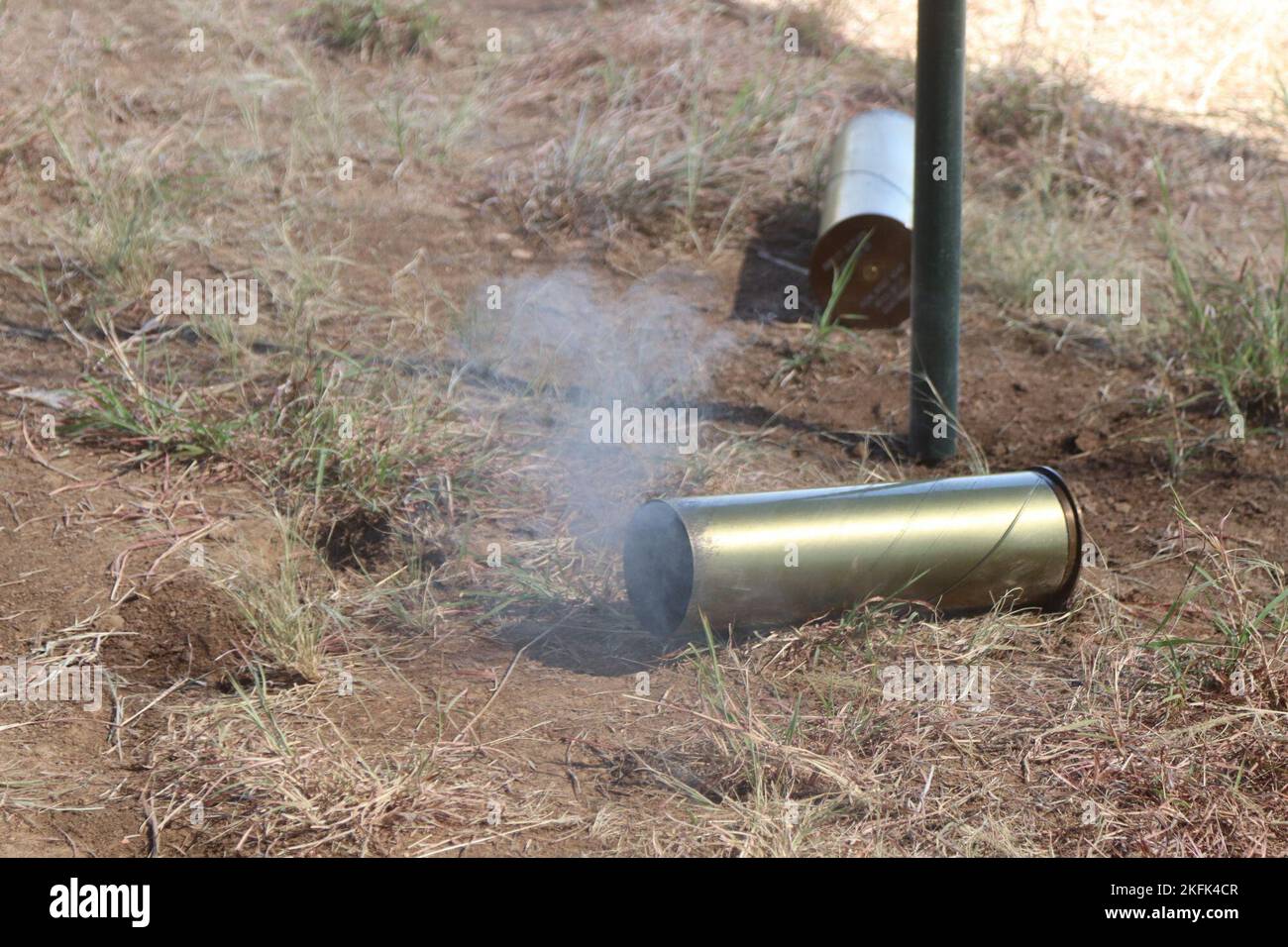 A smoking casing from a 105 mm howitzer round lands on the ground ...