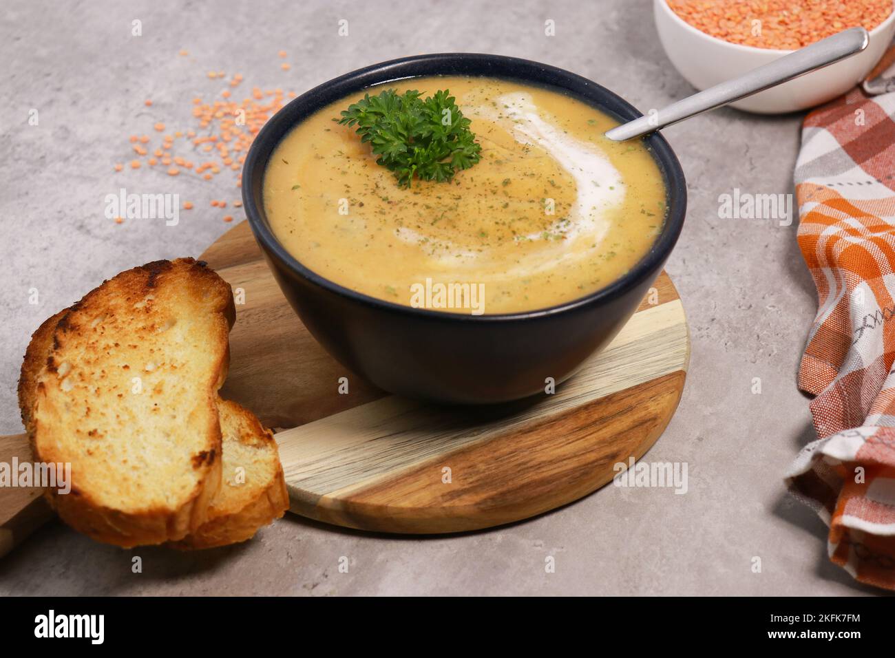 red lentils soup puree in dark bowl with bread on grey marble table ...