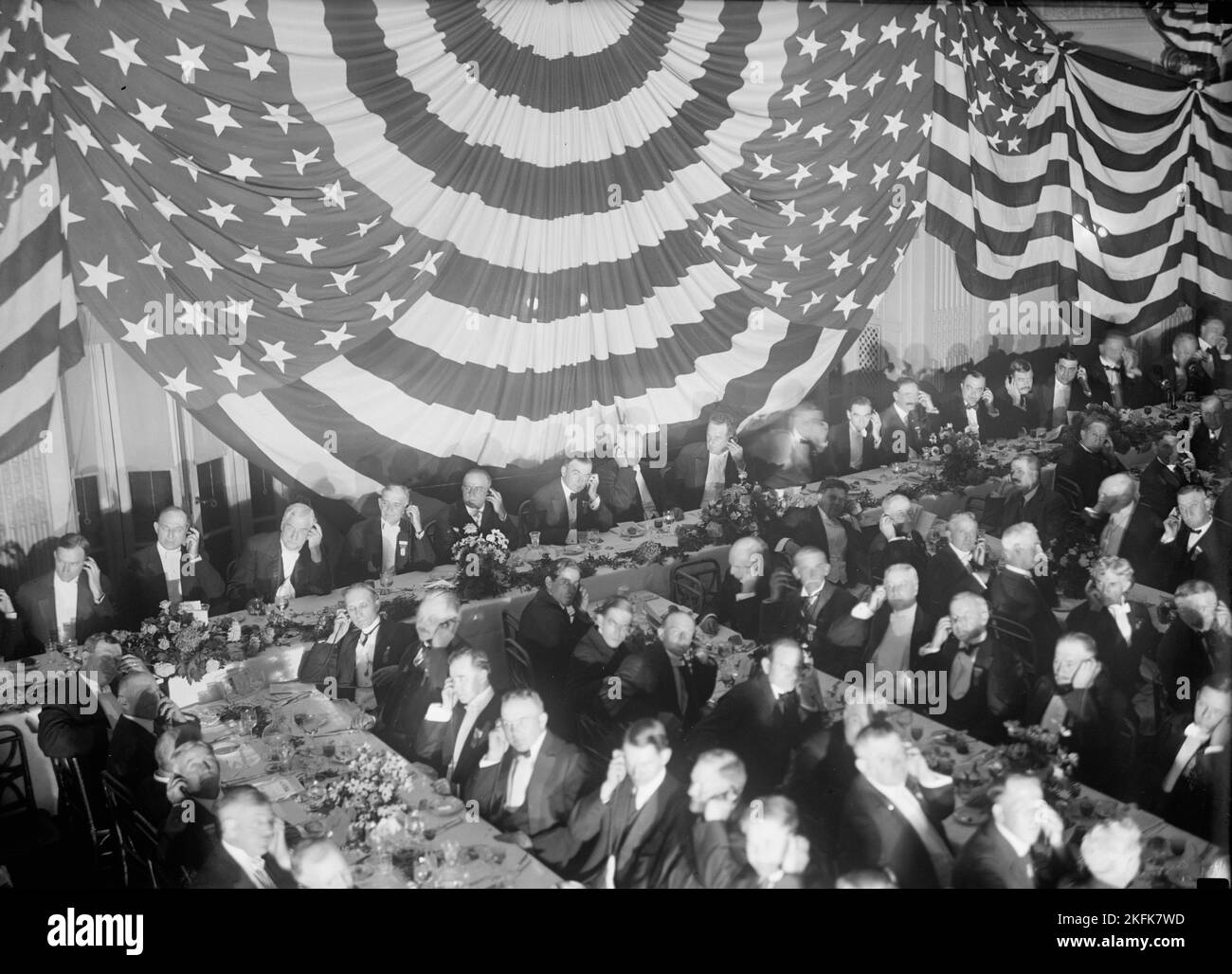 Banquet Scene with Flag Draping And Men Seated Holding Up Listening ...