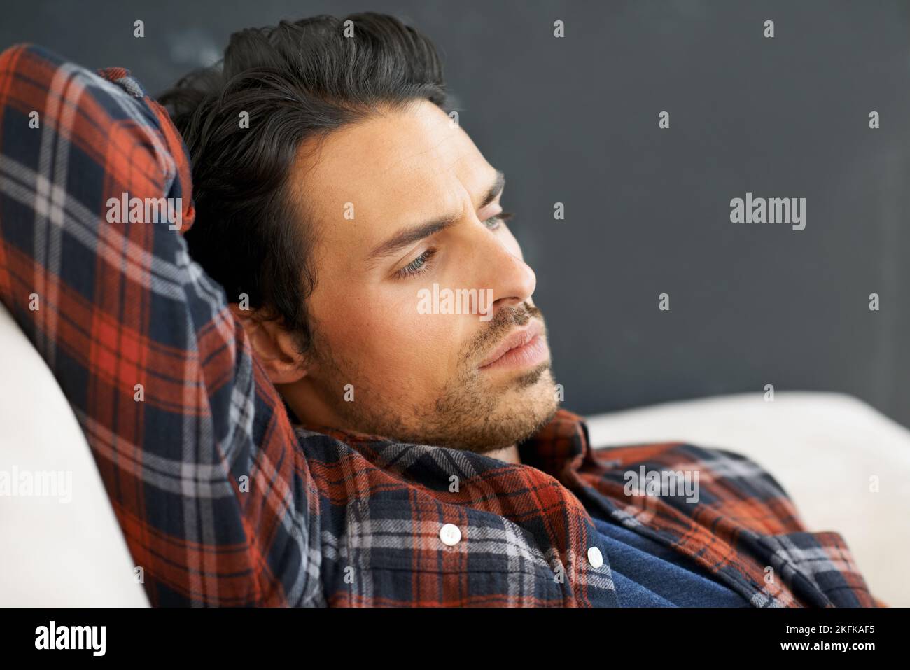 Feeling broody and moody. A gorgeous young man lying on a sofa with arm ...