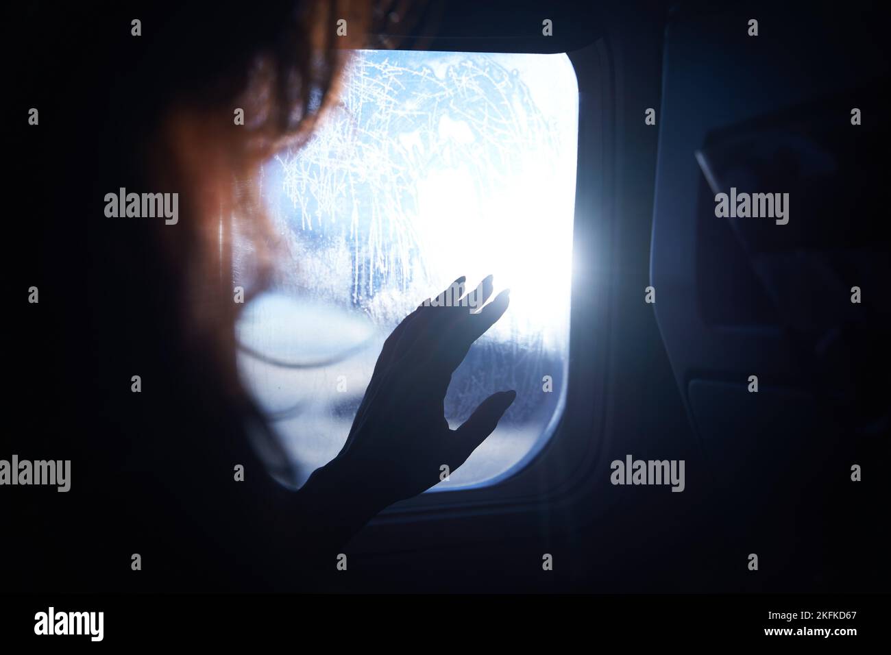 Female hand touches the warm sun rays from airplane window. Woman ...