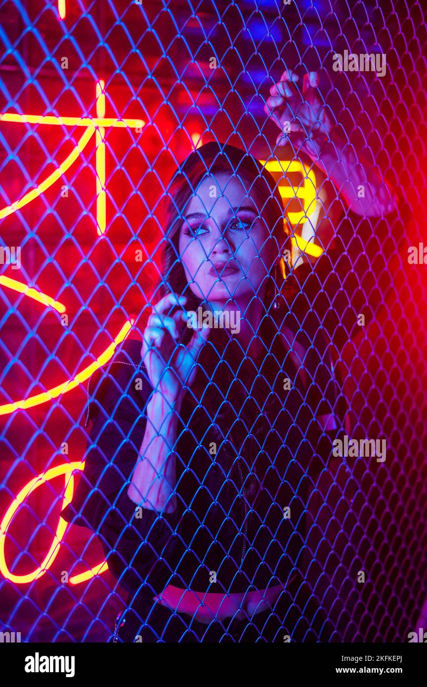 Caucasian woman in neon studio behind chain-link mesh Stock Photo - Alamy