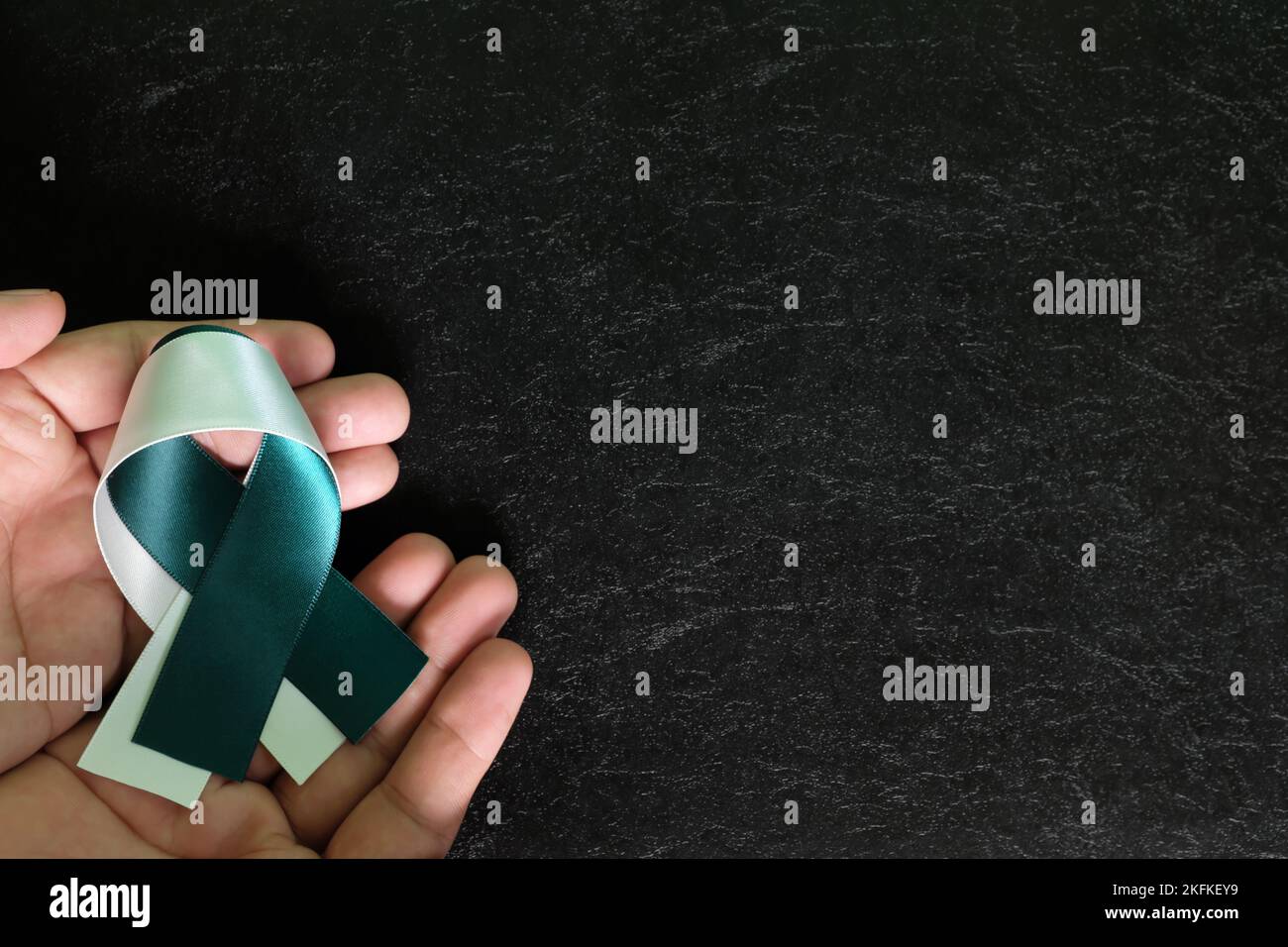 Top view of human hand palm holding teal and white ribbon in dark black ...
