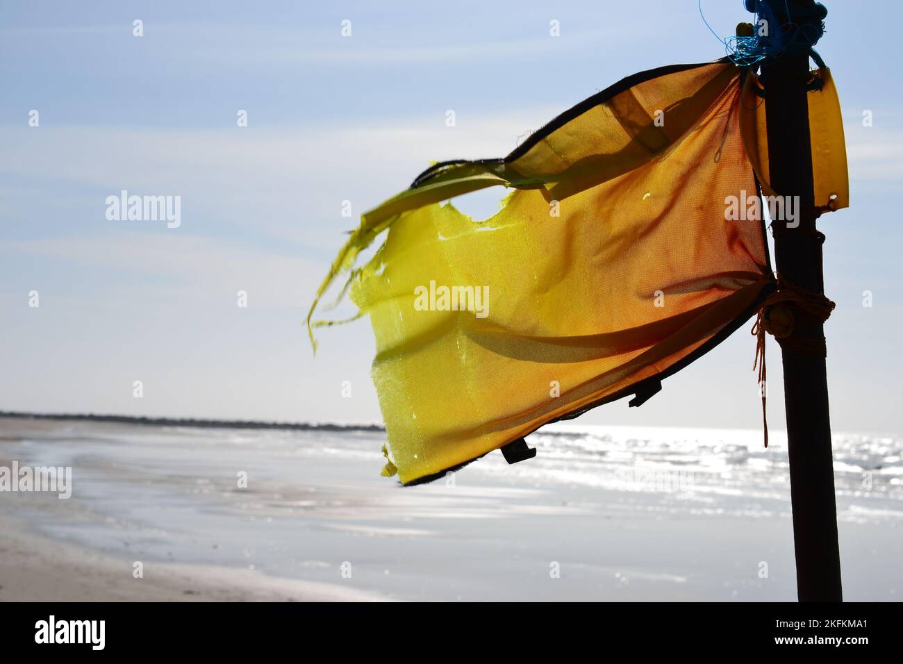 An old yellow flag on the pole waving in wind at the coast Stock Photo ...
