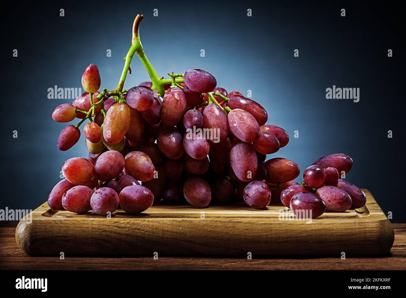 big bunch of rose grape on wooden cutting board and black gradient ...