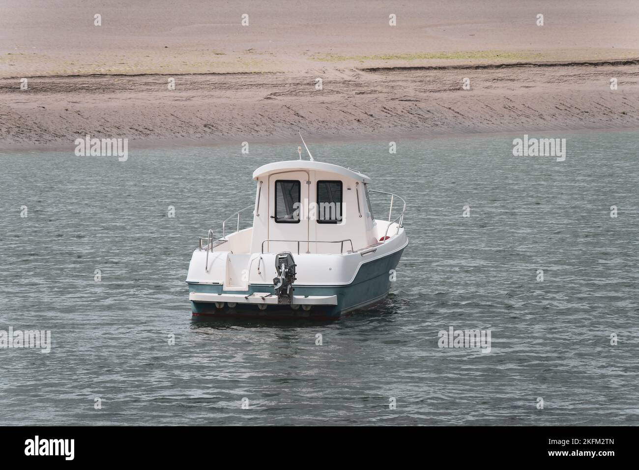A small motor boat is anchored on a calm water surface. Sandy beach ...