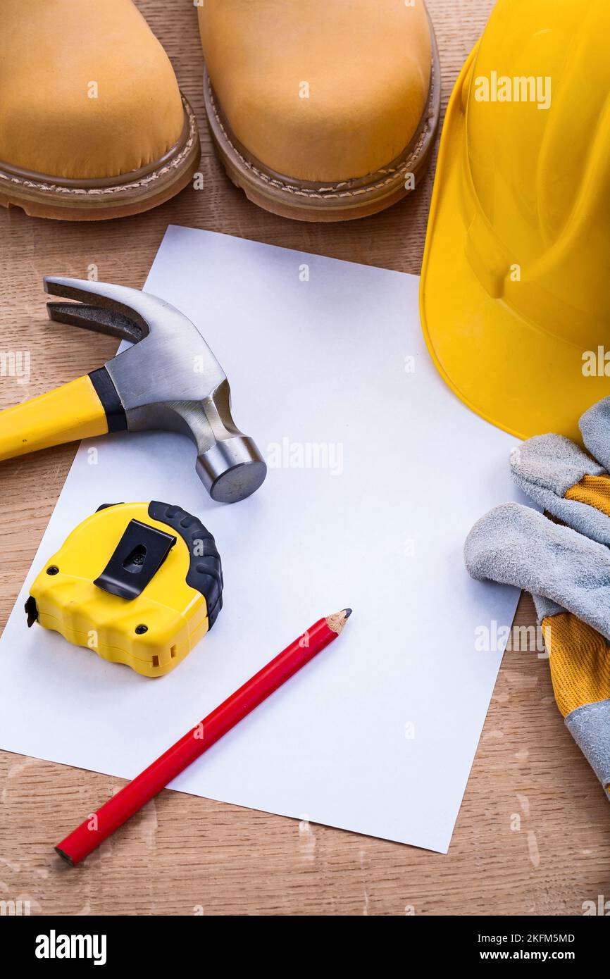 hammer and pencil tapeline sheet of paper gloves helmet boots on wooden ...