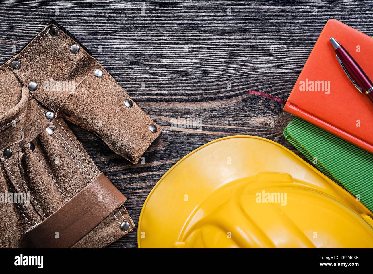 Leather building belt note-books pen yellow hard hat on wooden board ...