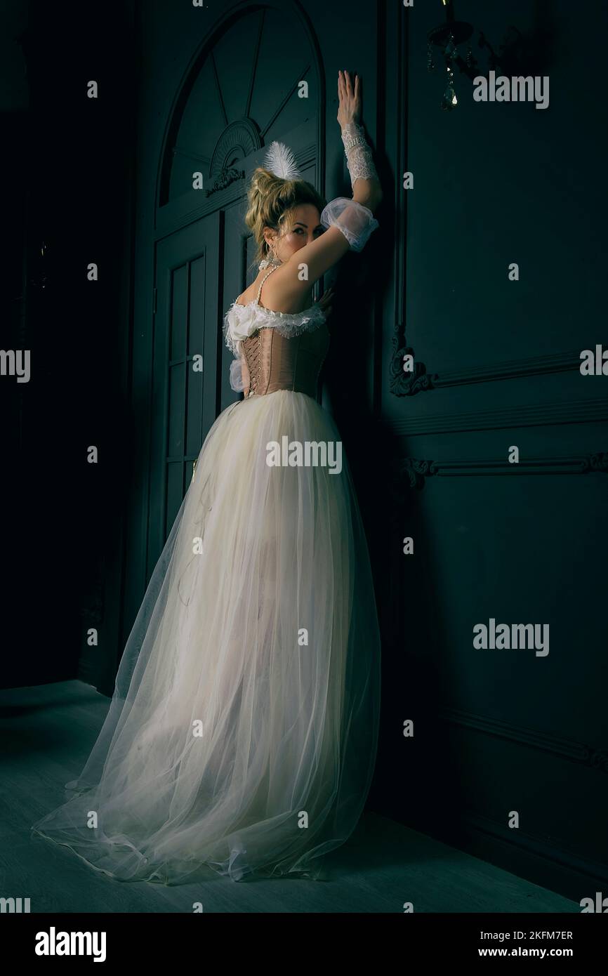 a young woman in an 18th century dress and lace stands against the wall ...