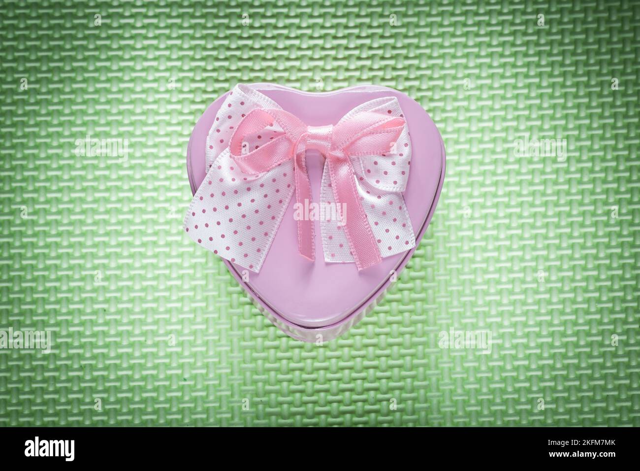 Metal pink heart-shaped present box with bow on green background ...