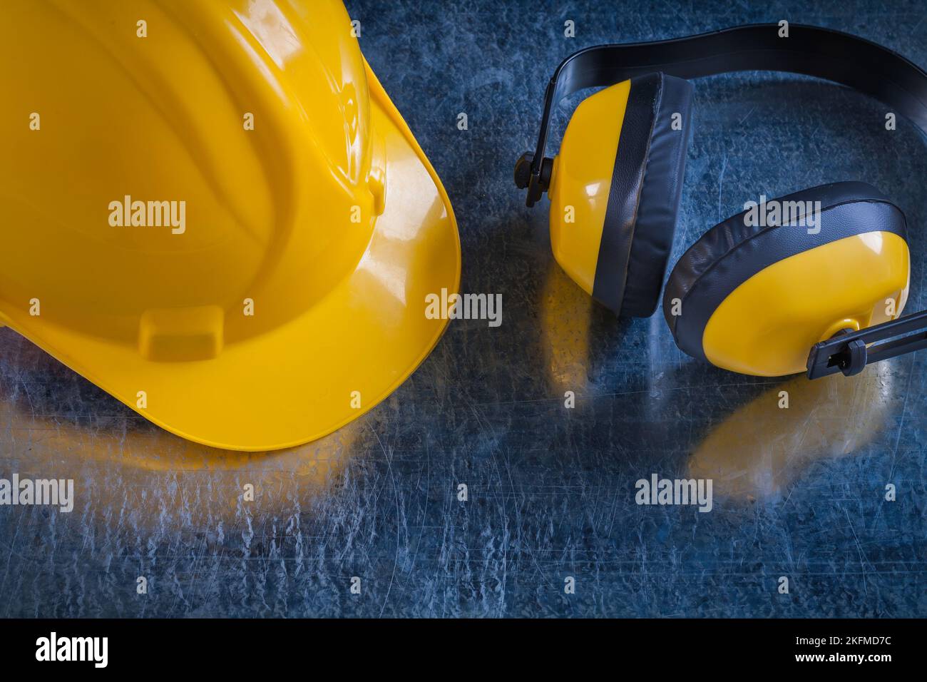 Safety yellow ear muffs and work helmet on scratched metallic ...