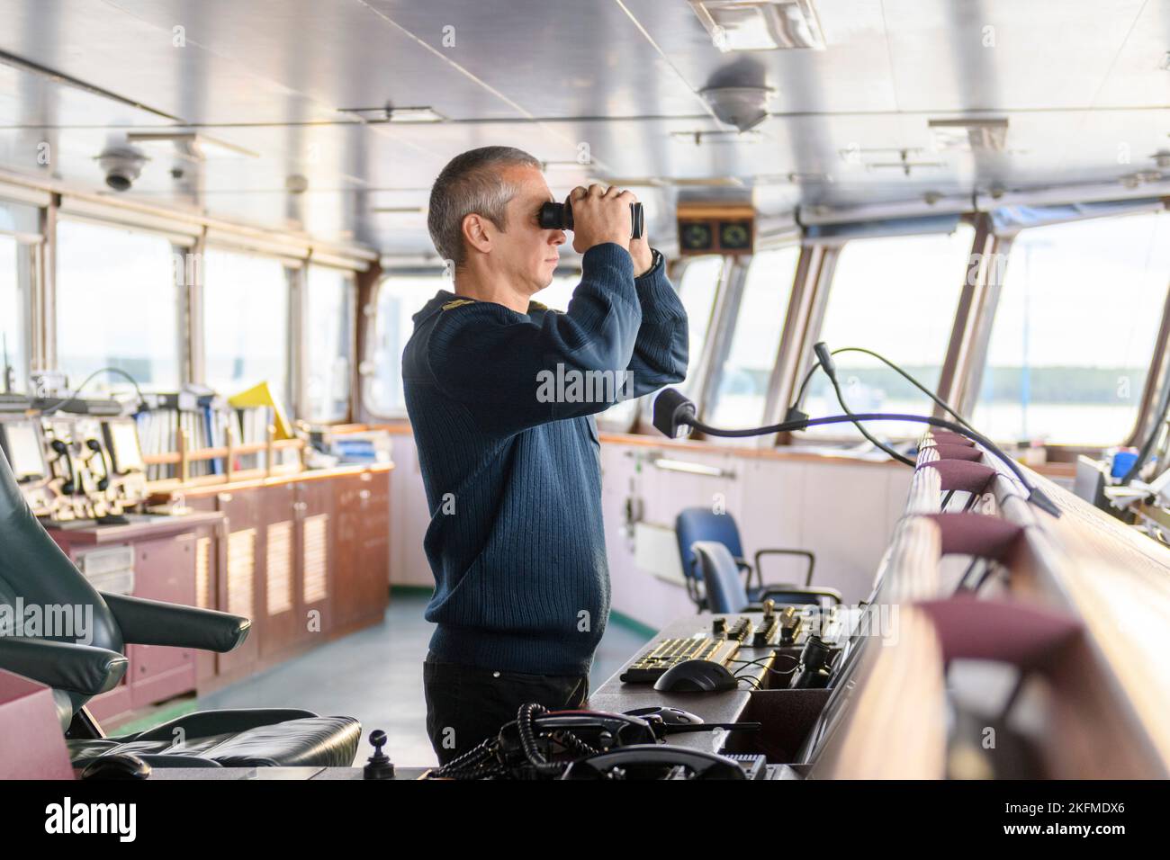 Deck officer with binoculars on navigational bridge. Seaman on board of ...