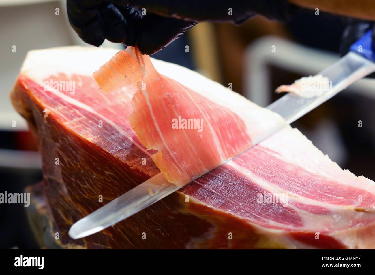 gloved hand of the butcher who with a sharp knife slices a slice of raw ...