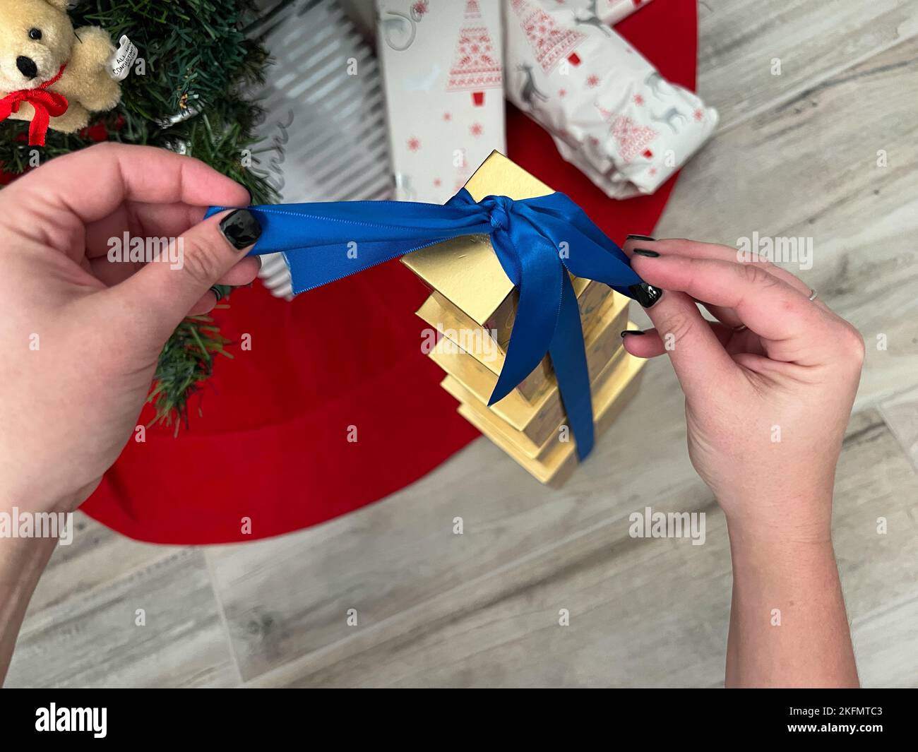 A girl unwrapping a Christmas present with gold boxes and a blue ribbon ...