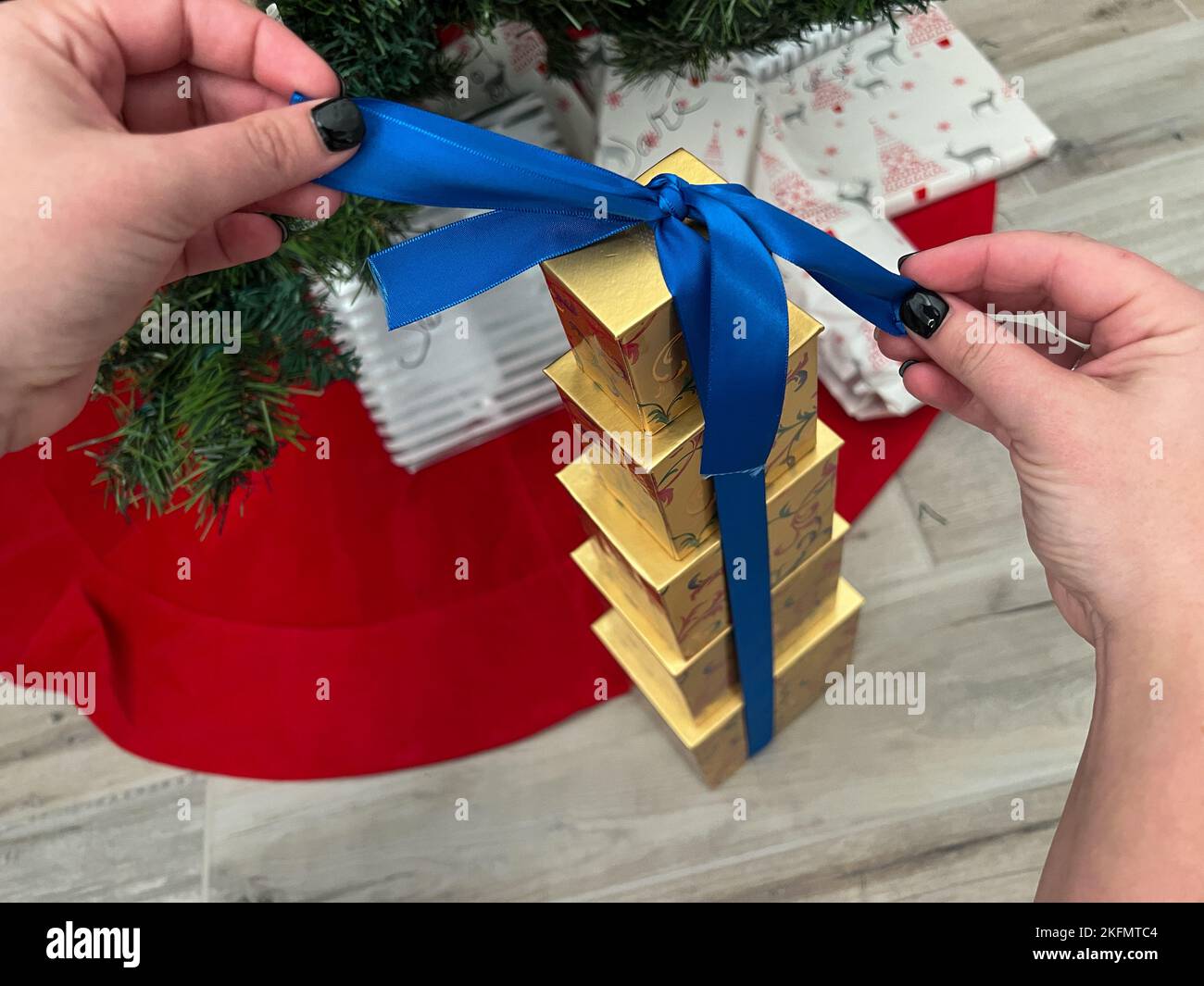 A girl unwrapping a Christmas present with gold boxes and a blue ribbon ...