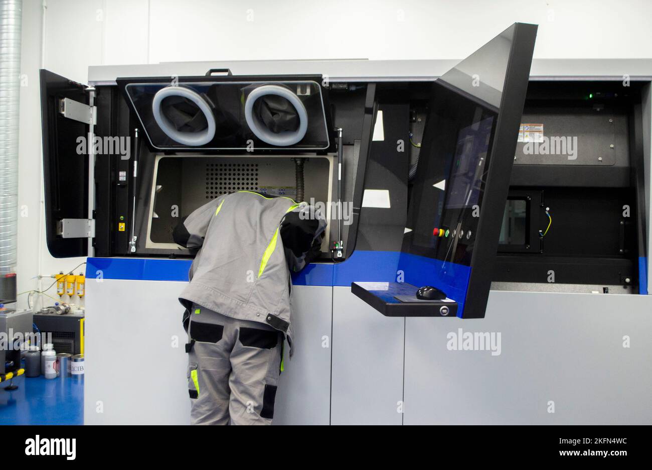 A worker looks into open window of inside large industrial 3D printer ...