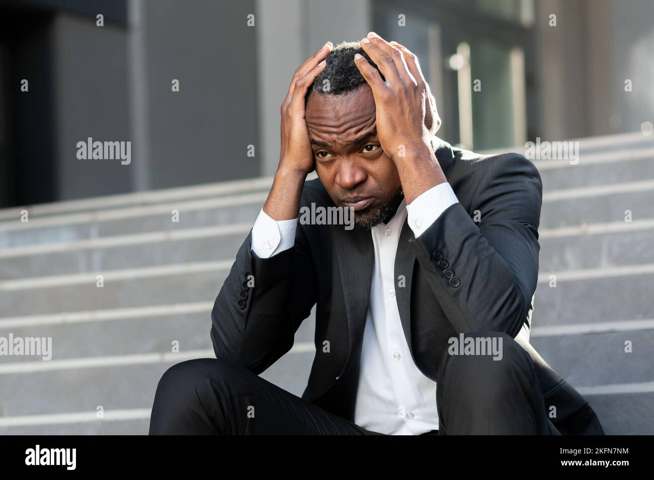 Upset and fired office worker sitting on stairs outside office building ...