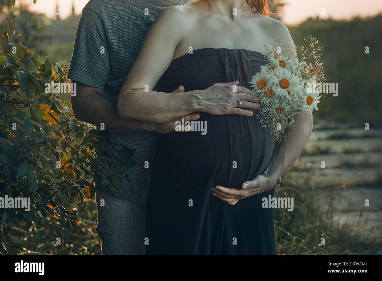 Pregnant woman and her husband hugging her tummy standing outdoors ...