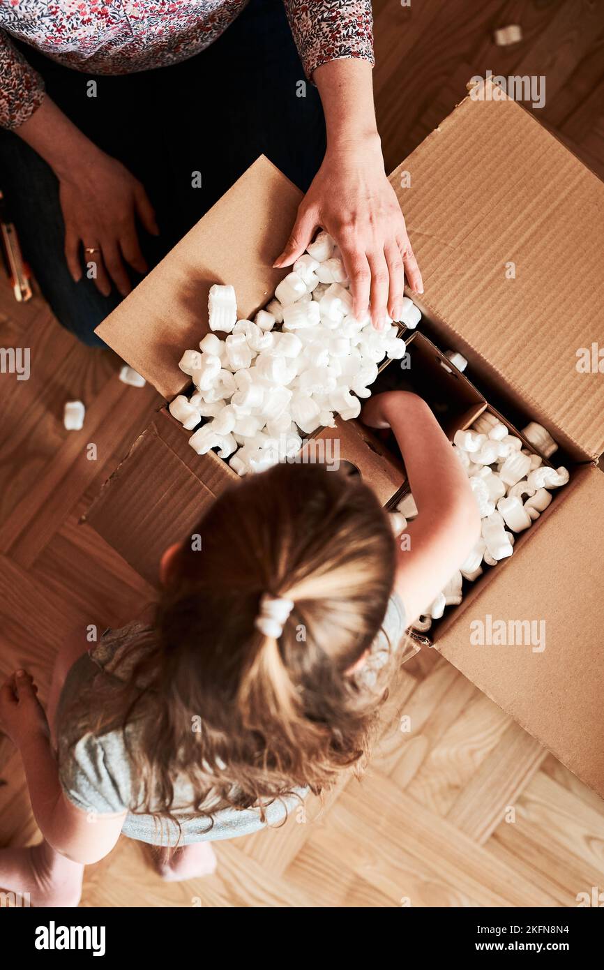 Woman unpacking a cardboard box parcel in room at home. Little girl ...