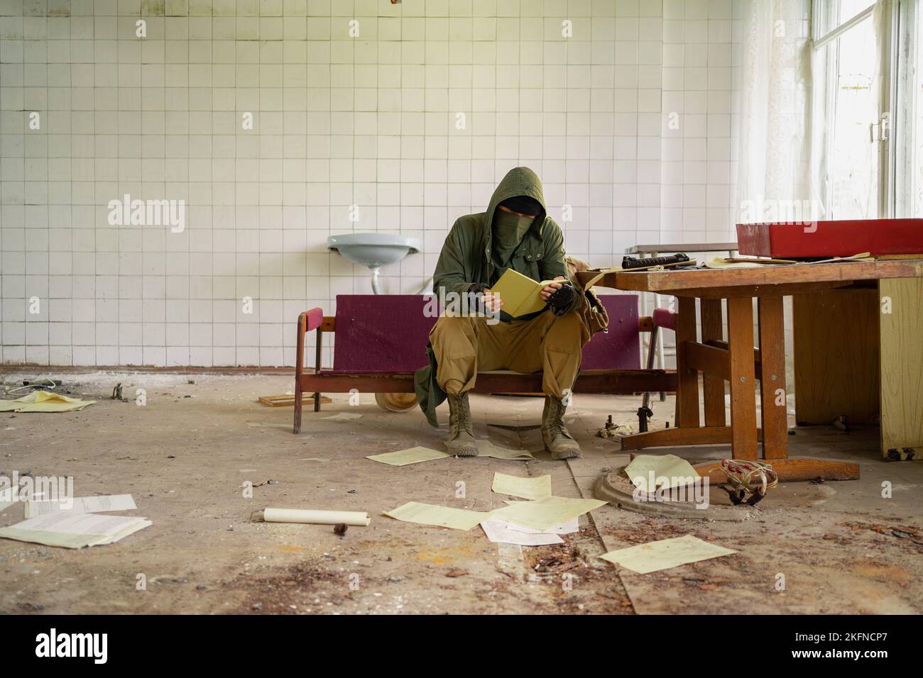 Man in bandana mask, hood and camo pants sits inside of abandoned ...