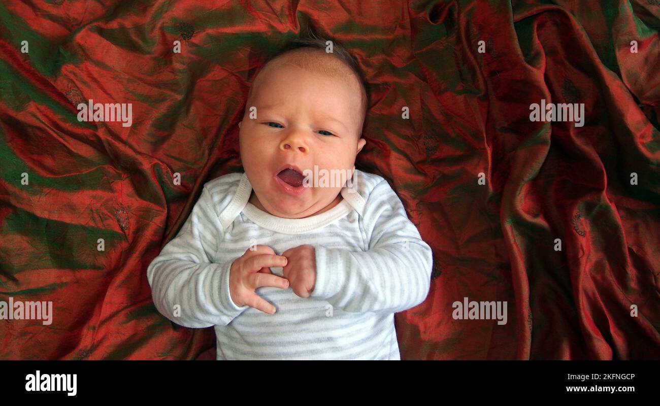 Yawning baby portrait on red silk shawl background Stock Photo - Alamy