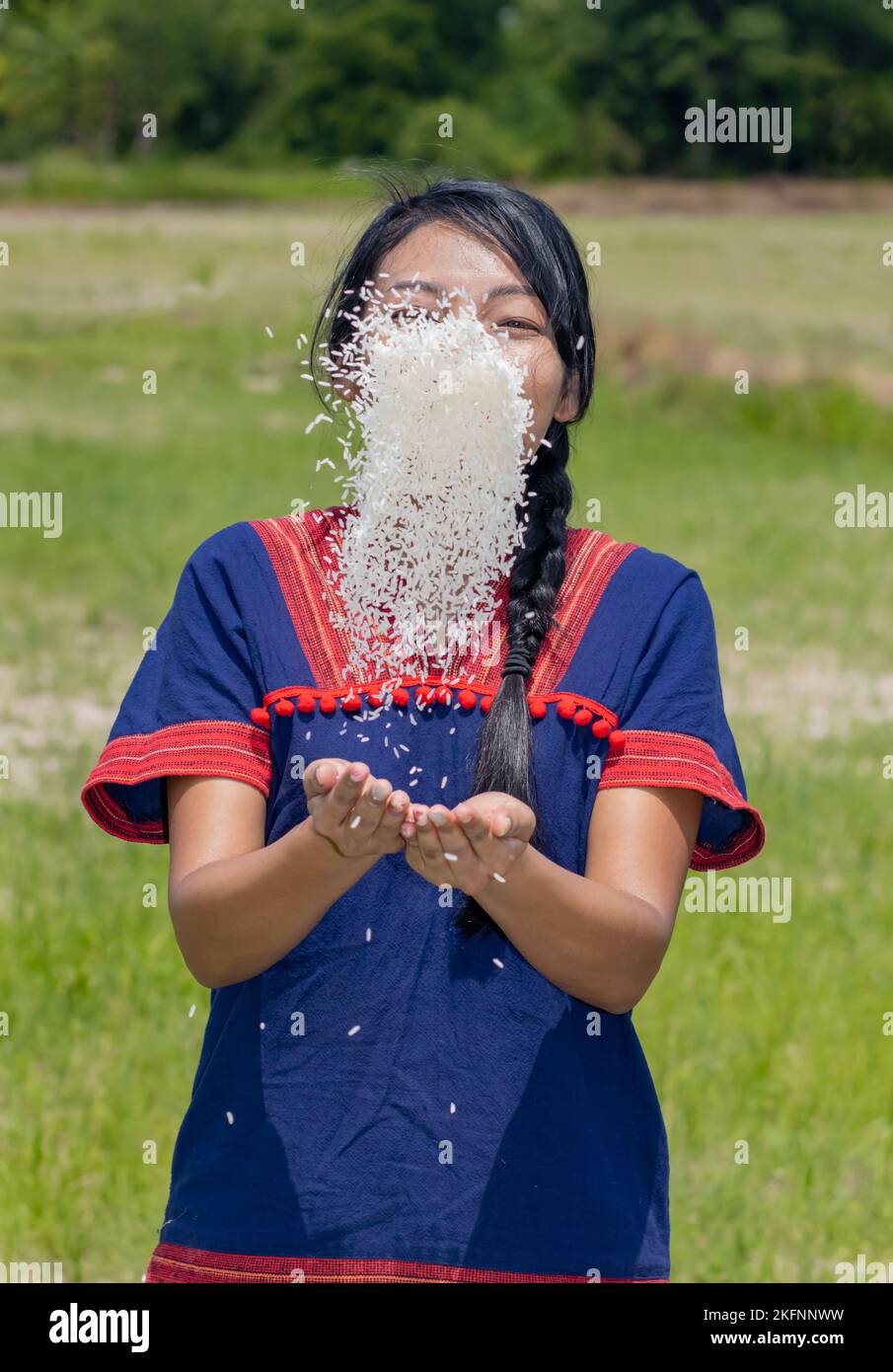Asian girl in traditional dress stands in a field and throws a handful ...