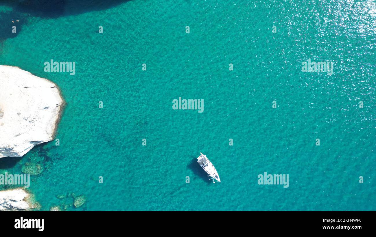 A bird's eye view of a white boat sailing on crystal-clear blue water ...