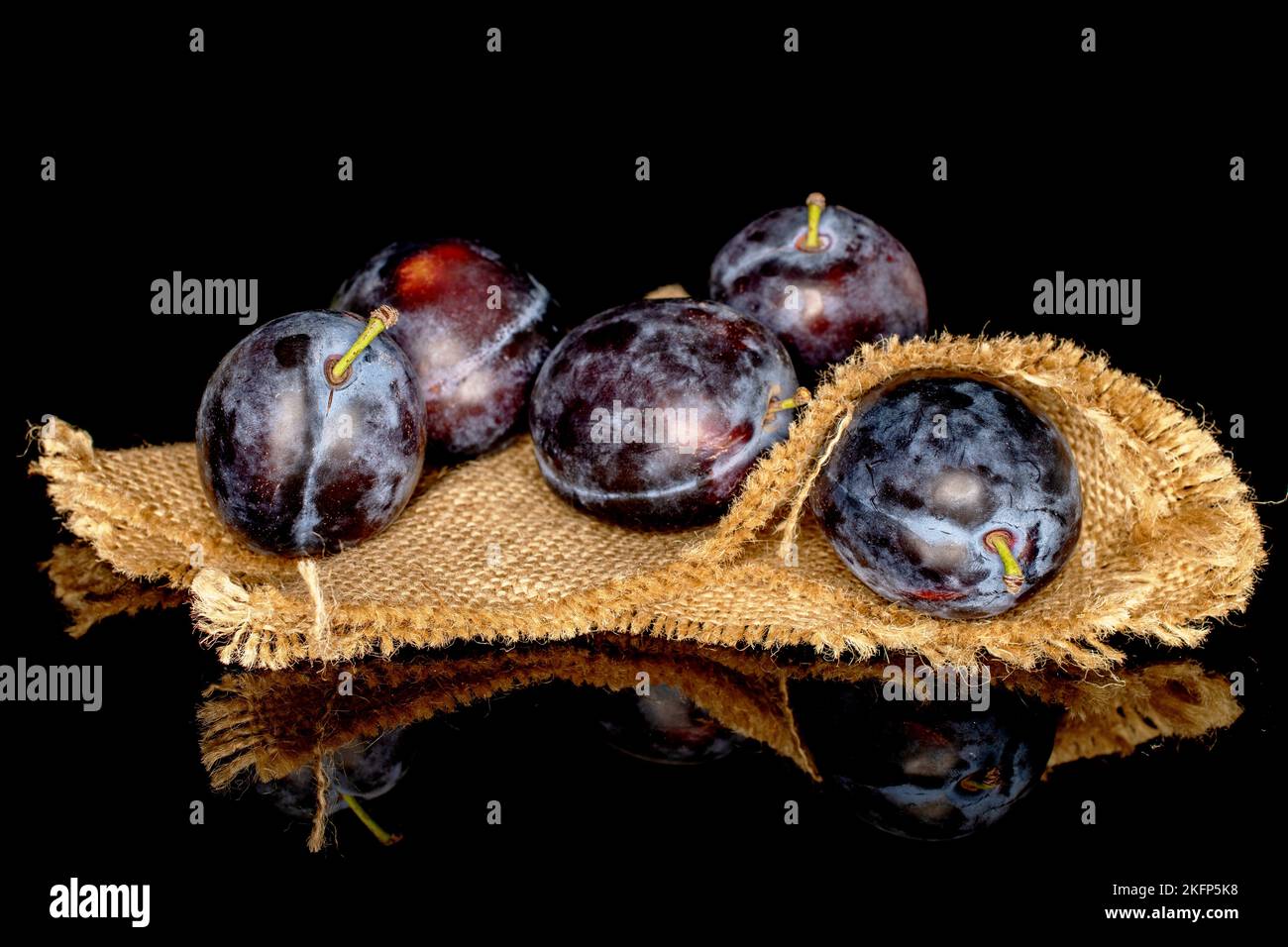 Several ripe dark purple plums on a jute fabric, close-up, isolated on ...